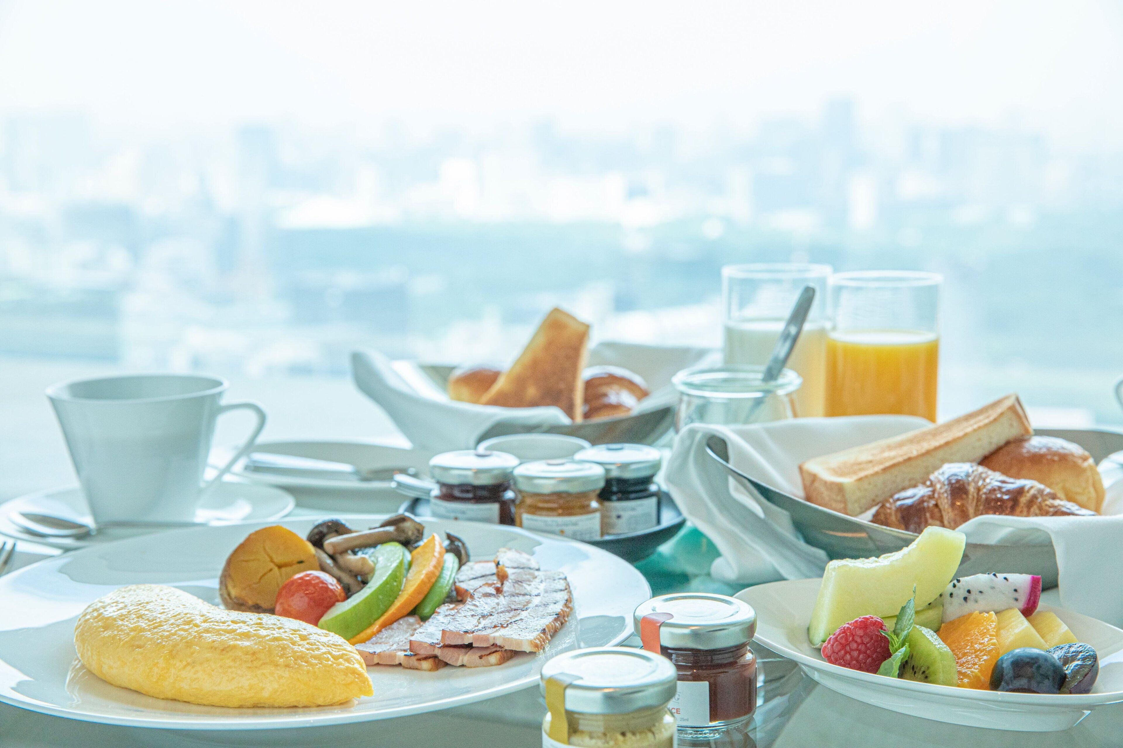 Disposição de café da manhã com diversos alimentos e acompanhamentos em pratos, uma xícara e um copo de suco de laranja.