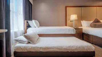 Quarto de hotel com duas camas, uma mesa de cabeceira com abajur e uma janela grande com cortinas.