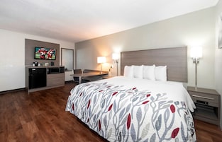 Quarto de hotel com cama, escrivaninha, televisão e espelho.