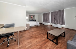 Quarto de hotel com cama, escrivaninha, cadeira, mesa, televisão e janela com cortinas.