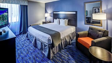 Quarto de hotel com uma cama grande, uma escrivaninha com computador, uma cadeira, um sofá e um espelho.