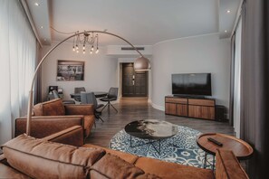 Uma sala de estar moderna com sofás de couro, uma mesa de centro redonda, uma televisão e um lustre de design exclusivo.