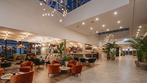 Um lobby espaçoso com assentos modernos, área de bar e grandes janelas com vista para a cidade.