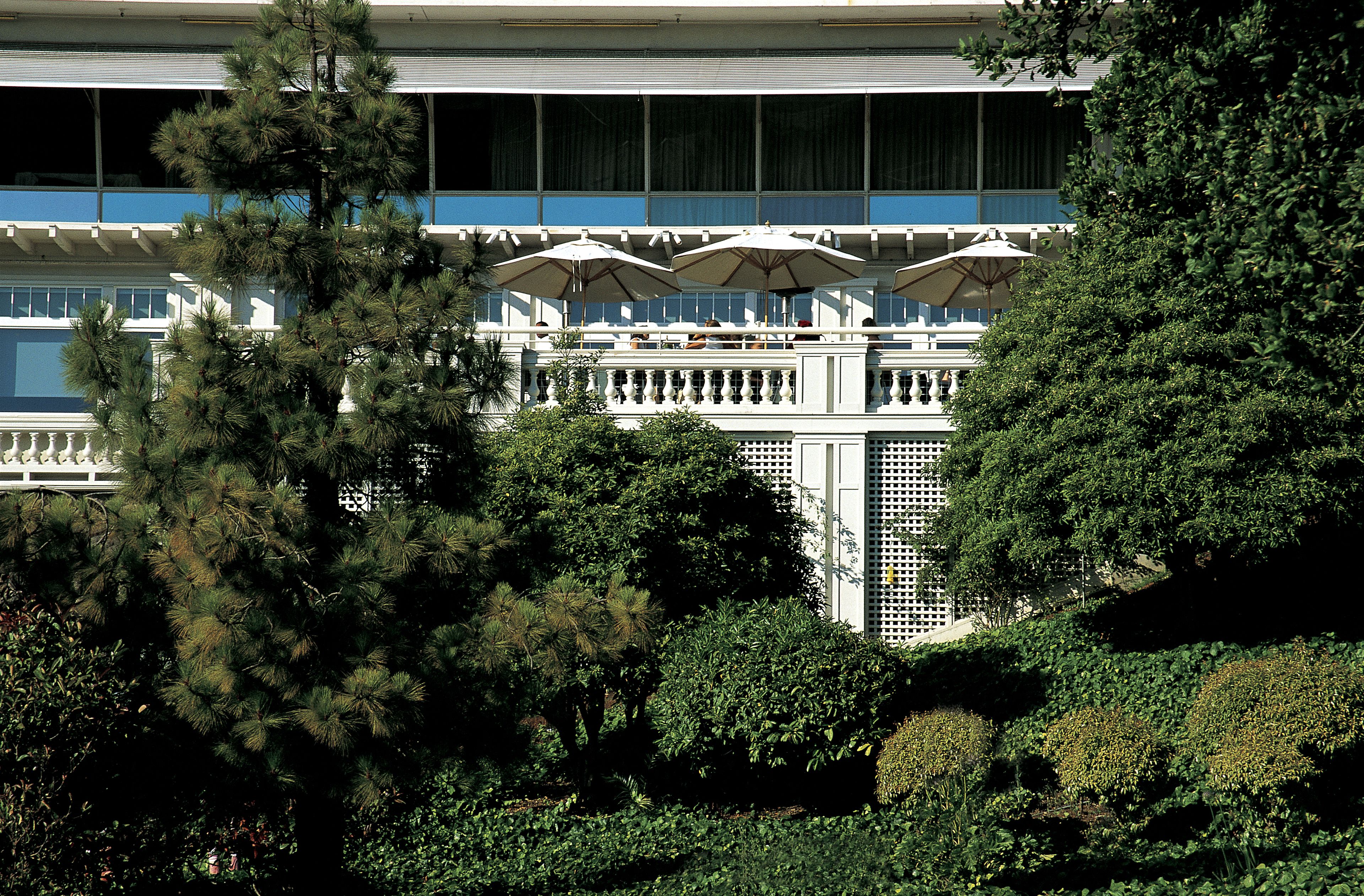 Hotel com varanda, guarda-sóis e vegetação exuberante.