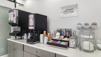 Uma estação de café com um dispensador de marca, copos de papel e uma placa com a inscrição 'Dream Cup'.