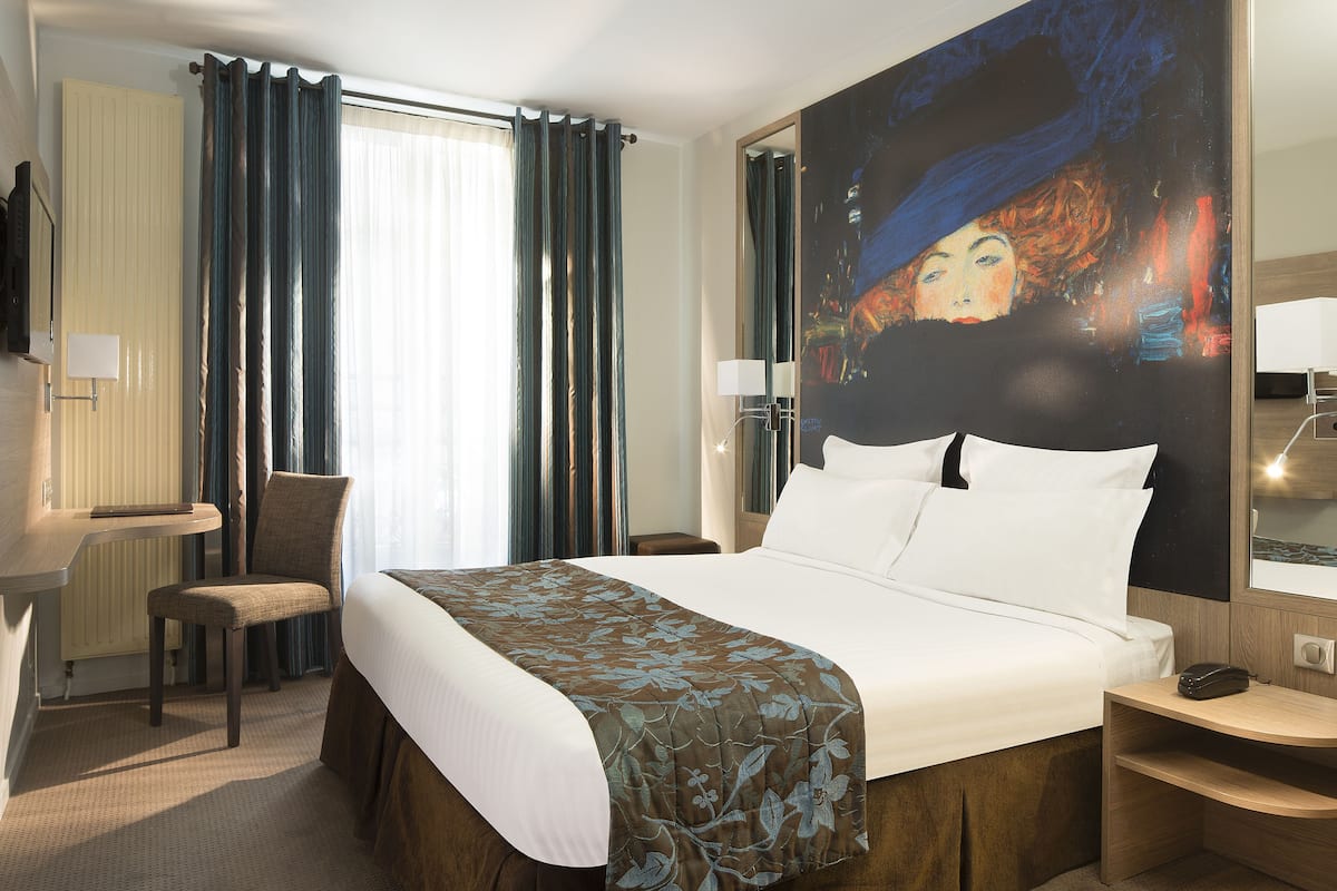 Quarto de hotel com uma cama grande, uma escrivaninha, uma cadeira e um quadro na parede.