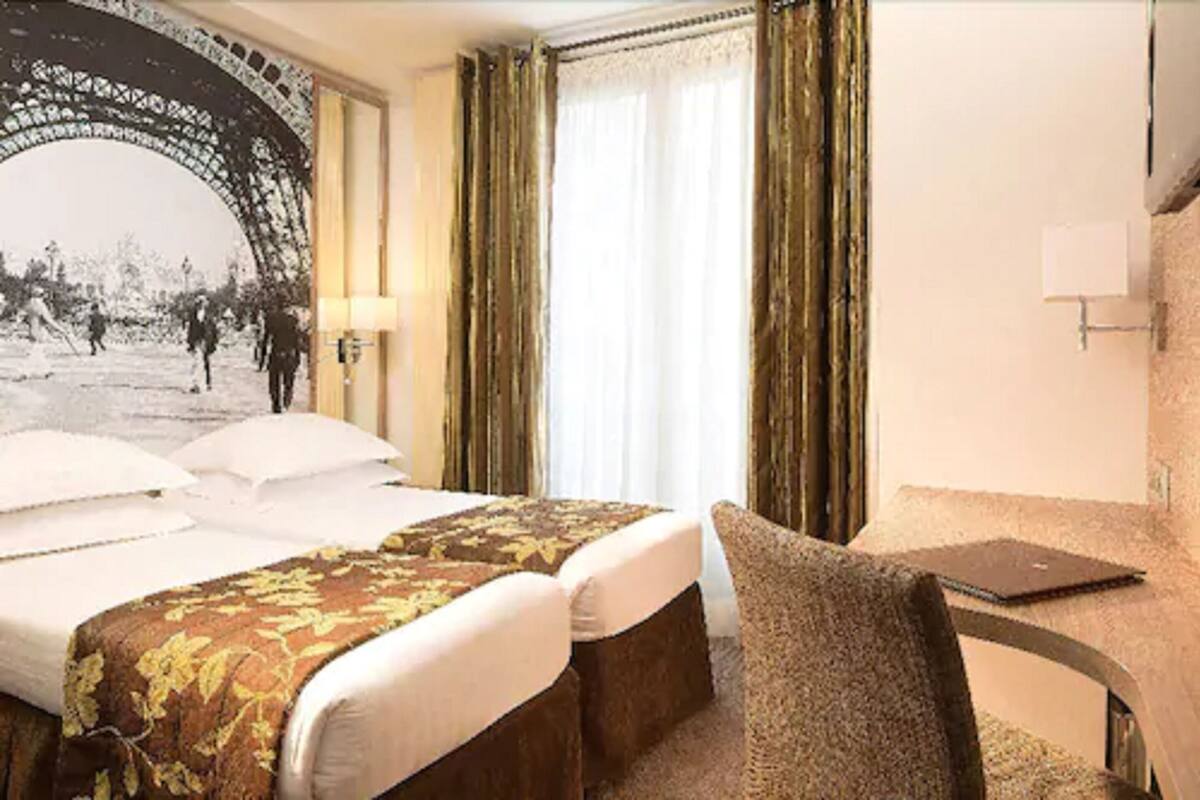 Quarto de hotel com uma cama, uma cadeira, uma mesa e uma janela grande com cortinas.
