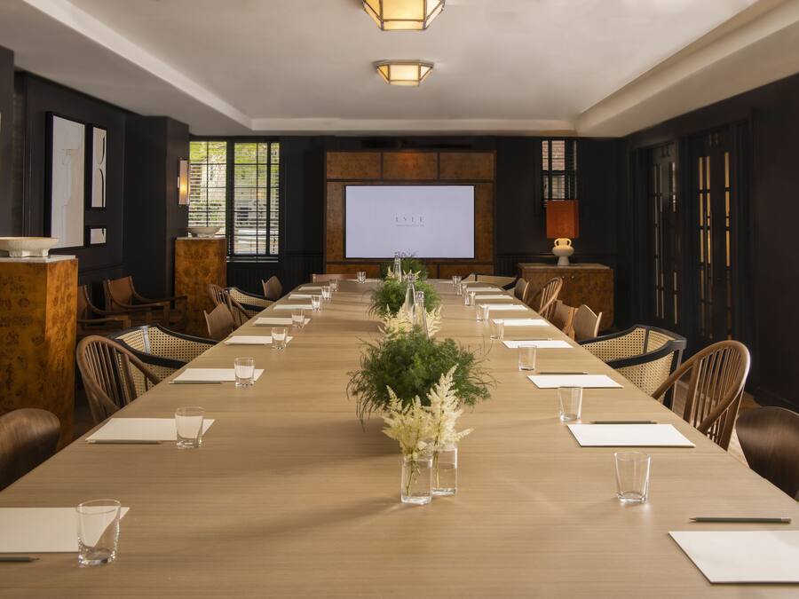 Uma sala de conferência com uma mesa comprida, cadeiras e uma tela de projetor exibindo "LYLE".