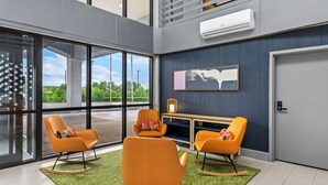 Quarto moderno com grandes janelas, poltronas de balanço laranja, uma mesinha e um quadro na parede.