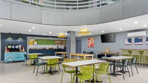 Uma cafeteria moderna com cadeiras e mesas verdes, um balcão com alimentos e uma TV fixada na parede.