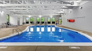 Uma grande piscina interior com pistas demarcadas, uma cadeira de salva-vidas e vista para o exterior por grandes janelas.