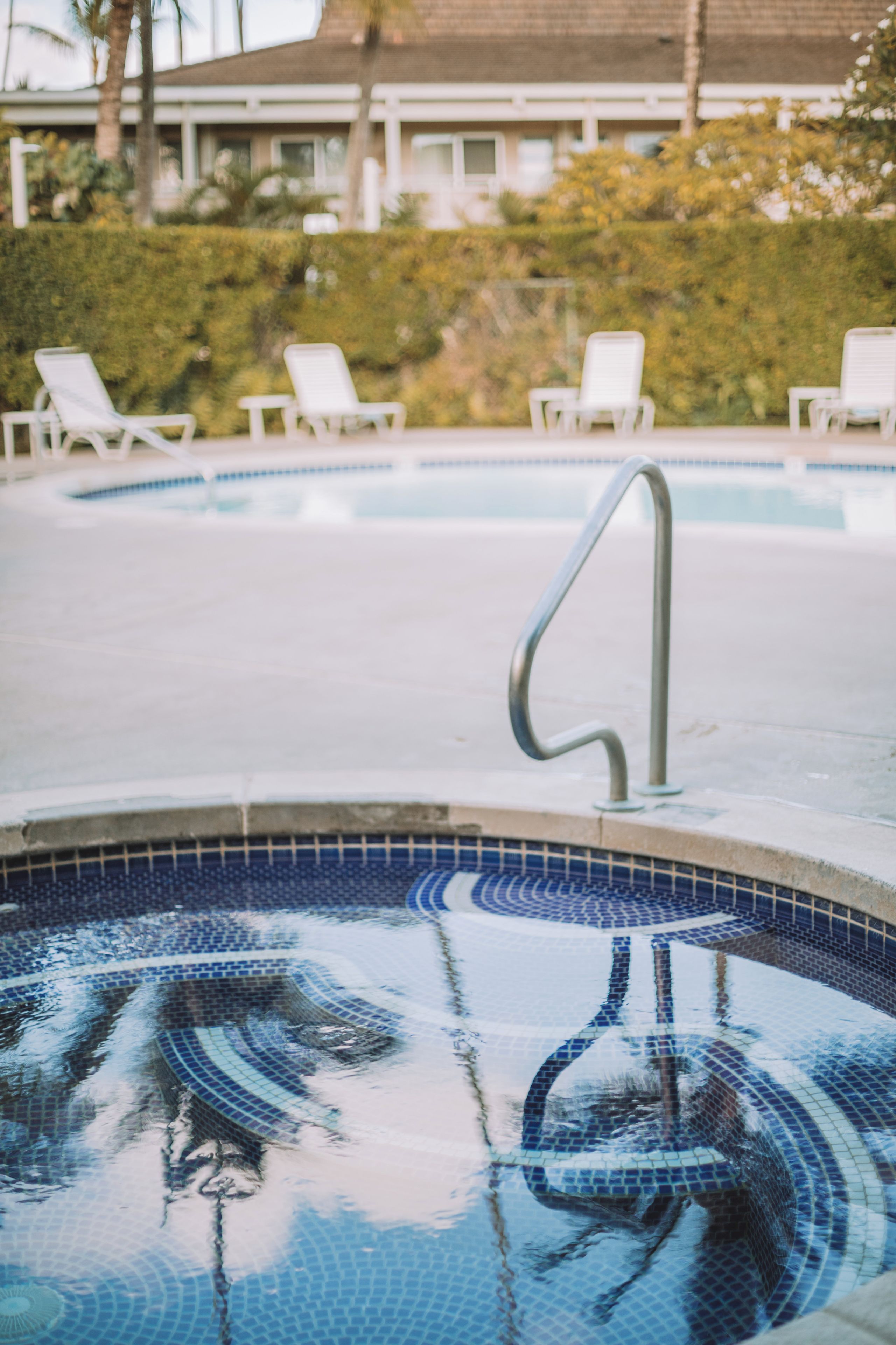 Piscina com plataforma de mergulho, cadeiras de descanso e um edifício ao fundo.
