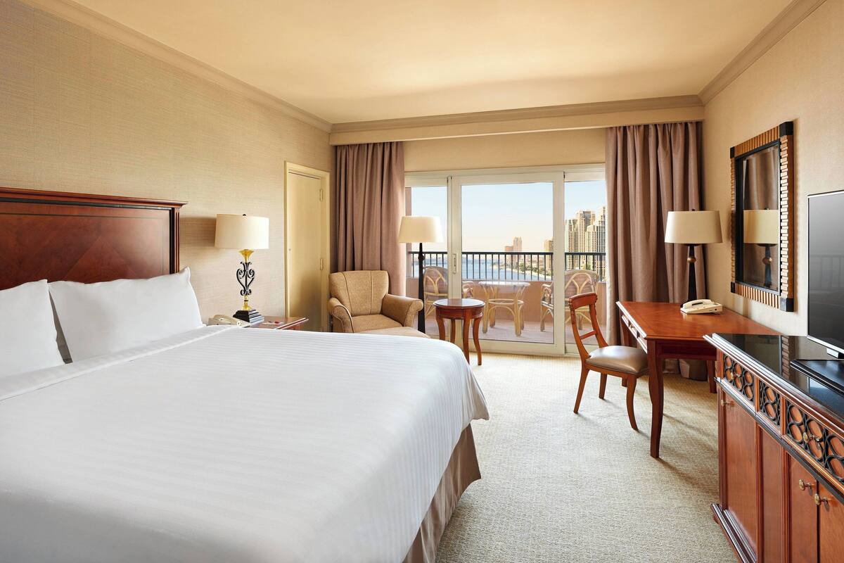 Quarto de hotel com uma cama grande, uma escrivaninha, uma cadeira, televisão e varanda com vista.