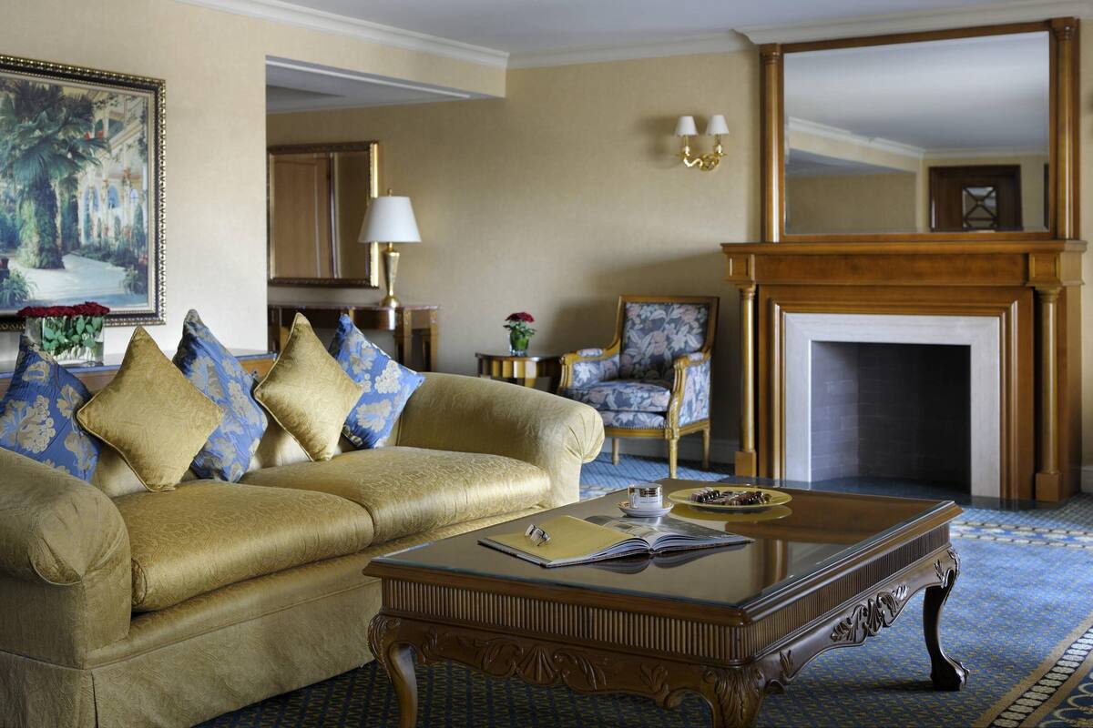 Quarto com sofá dourado, mesa de centro de madeira, quadro emoldurado, luminária e lareira.
