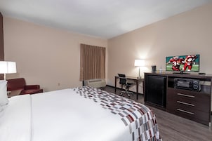 Quarto de hotel com cama, escrivaninha, cadeira, televisão e minibar.