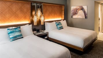 Quarto de hotel com duas camas, uma mesa de cabeceira, uma luminária e um quadro na parede.