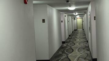 Corredor comprido e estreito de hotel, com carpete estampado, paredes brancas e portas numeradas 117 e 118.