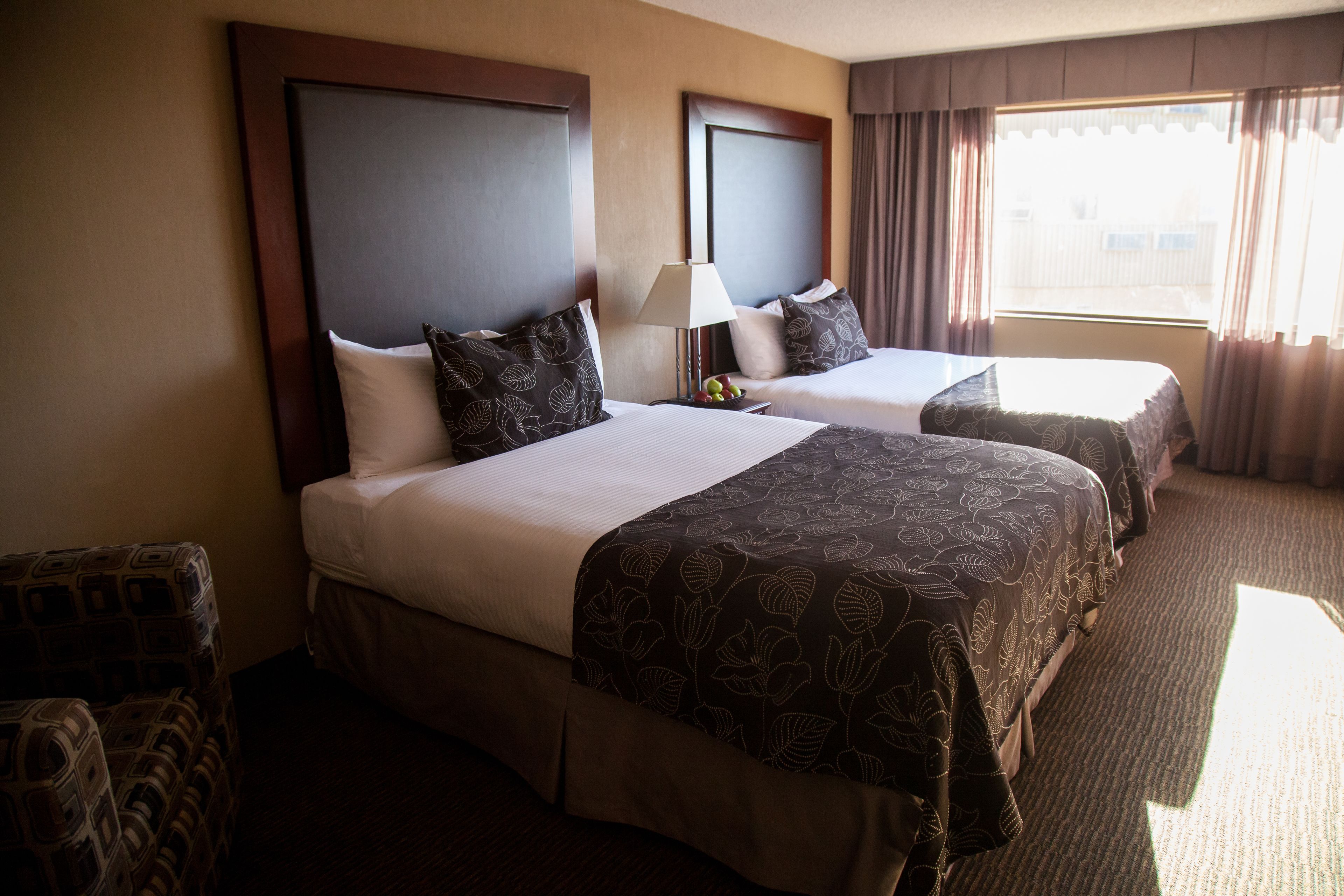 Quarto de hotel com duas camas, mesa de cabeceira com abajur e vista da cidade pela janela.