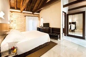Quarto de hotel com cama grande, televisão, guarda-roupa e parede de pedra.
