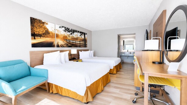 Quarto de hotel com cama, escrivaninha, cadeira, sofá e uma grande pintura na parede.