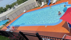 Piscina com borda azul, cercada por um deck laranja e cadeiras de descanso brancas.