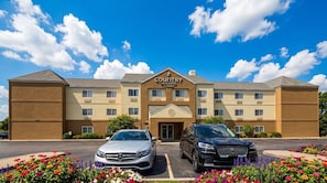 Um hotel Country Inn & Suites com estrutura em dois andares, estacionamento e fachada arborizada com flores.