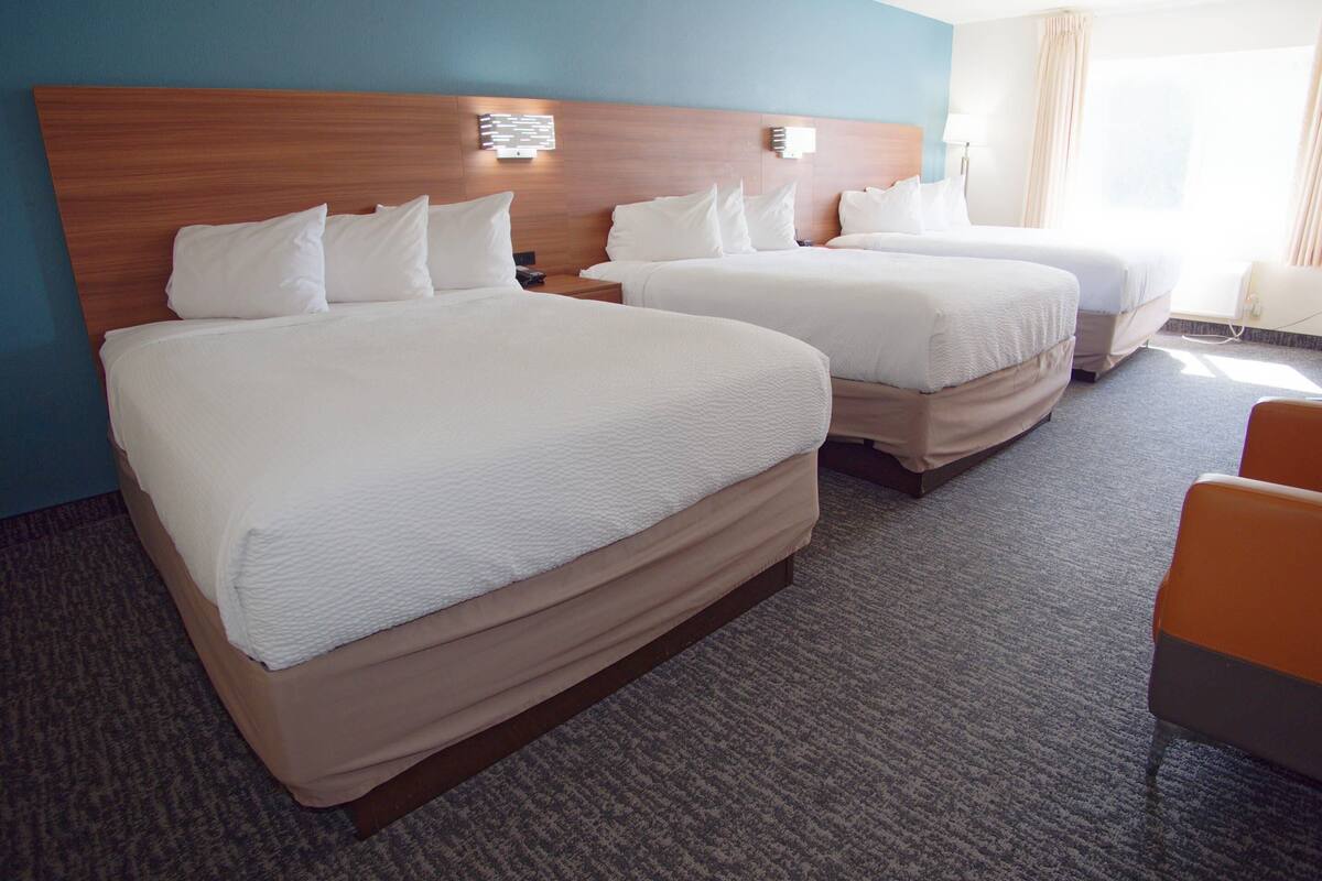 Quarto de hotel com duas camas, cabeceira de madeira, piso coberto por carpete e janela com cortinas.
