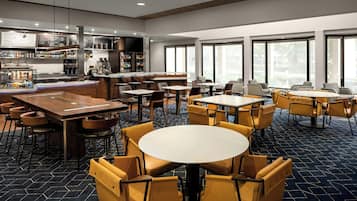 Um restaurante moderno com área de bar, diversas opções de assento, incluindo mesas redondas e cabines, e uma grande janela que oferece vista para o exterior.