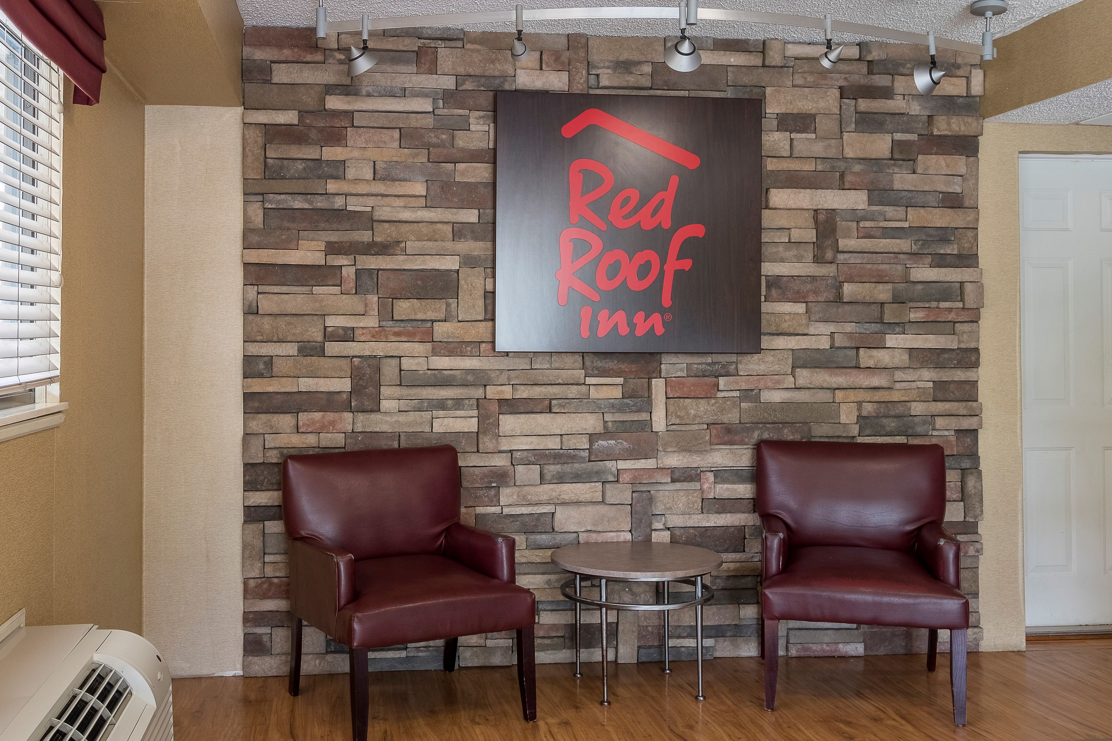 Placa Red Roof Inn em uma parede de pedra, com duas poltronas de couro e uma pequena mesa.