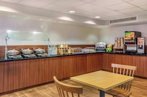 Uma mesa de pequeno-almoço com bancada de madeira, vitrine de vidro e máquina de café.