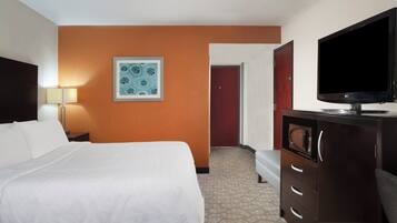 Quarto de hotel com uma cama, penteadeira, televisão, luminária e um quadro na parede.