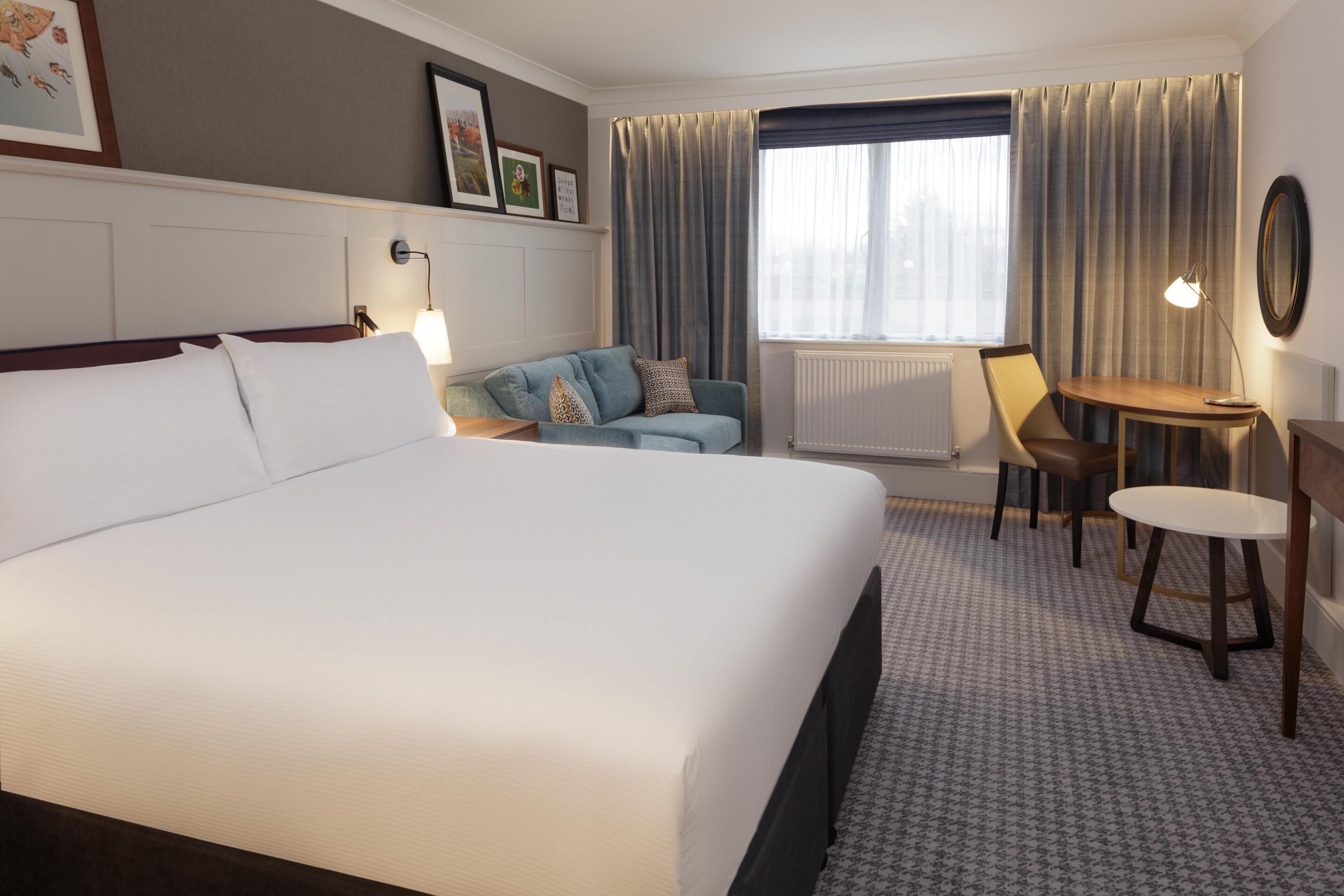 Quarto de hotel com uma cama grande, um sofá, uma mesa pequena e uma cadeira.