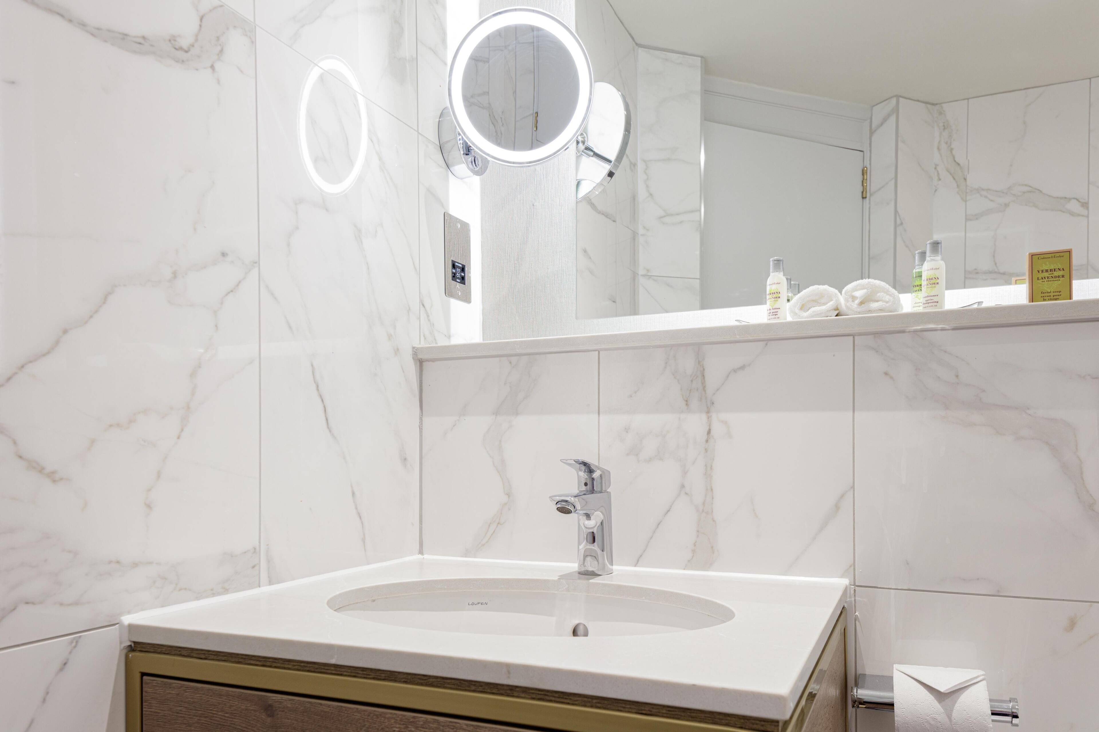 Casa de banho com lavatório de mármore, espelho e produtos de higiene pessoal numa prateleira.