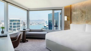 Quarto de hotel com uma grande janela, uma cama, área de estar com mesa e vista para a cidade.