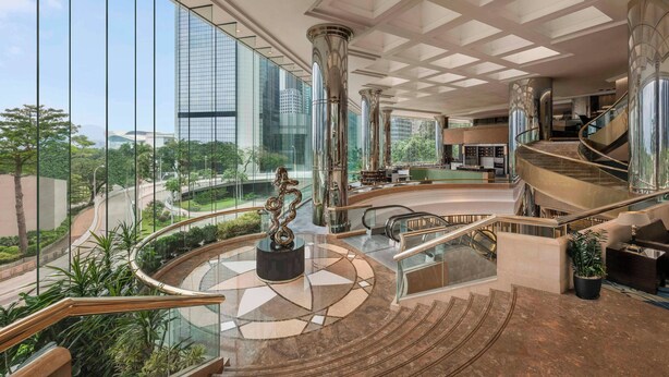 Um hall amplo com uma escultura central, uma escadaria em espiral e vista para a paisagem urbana ao redor.