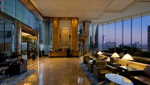 Um saguão de hotel com balcão de recepção, área de estar e grandes janelas com vista para a cidade.
