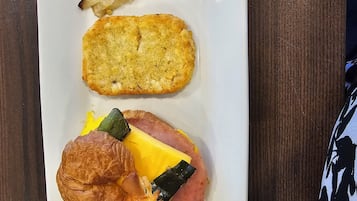 Um prato com um croissant, fiambre, queijo e legumes.