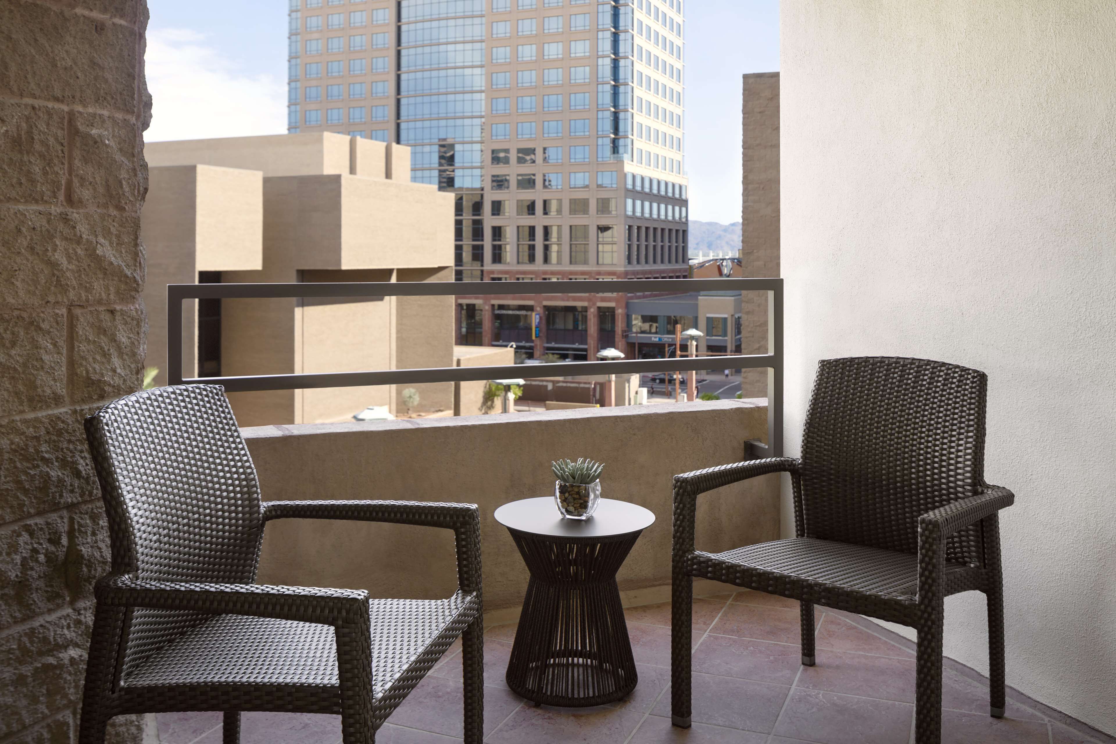 Varanda com duas cadeiras de vime e uma mesa pequena, com vista para um horizonte urbano com edifícios modernos.