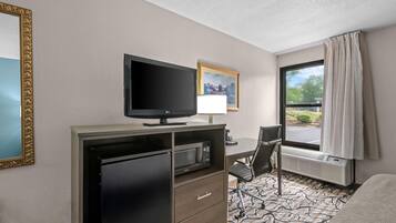 Quarto de hotel com televisão de tela plana, escrivaninha com cadeira, cama, janela com cortinas e carpete estampado.