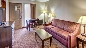 Quarto de hotel com sofá, mesa de centro, televisão, escrivaninha e uma cadeira.