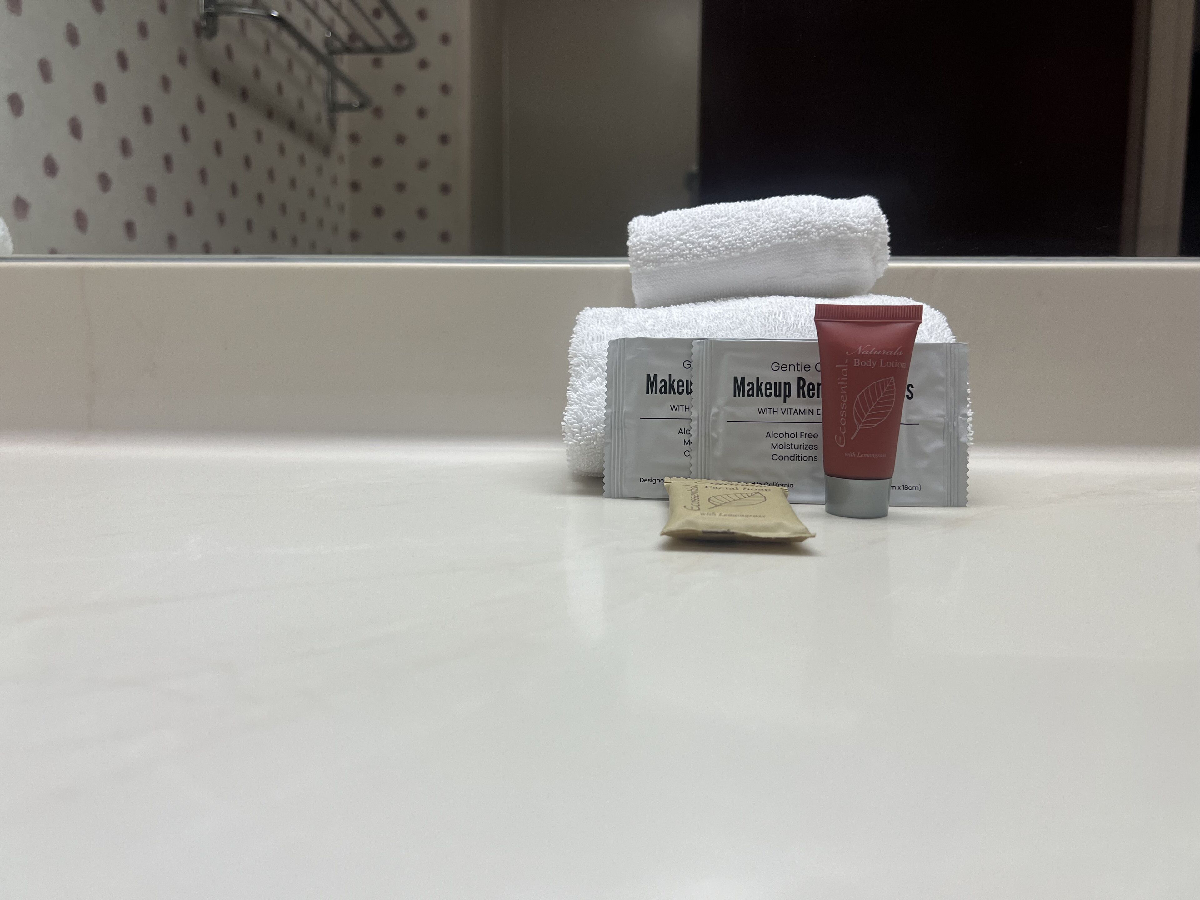 Uma bancada de banheiro com uma toalha branca, um tubo de loção corporal e uma caixa de demaquilante.