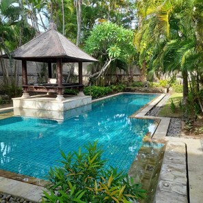 Uma piscina com um gazebo, cercada por vegetação exuberante e palmeiras.