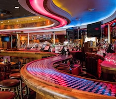 Um bar com balcão curvo, banquetas e diversos copos e garrafas.