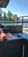 Terraço com mobiliário de vime e mesa de vidro, com vista para a água e um cais.
