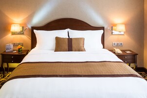 Quarto de hotel com uma cama grande, duas mesas de cabeceira, um criado-mudo, uma lâmpada e um telefone.