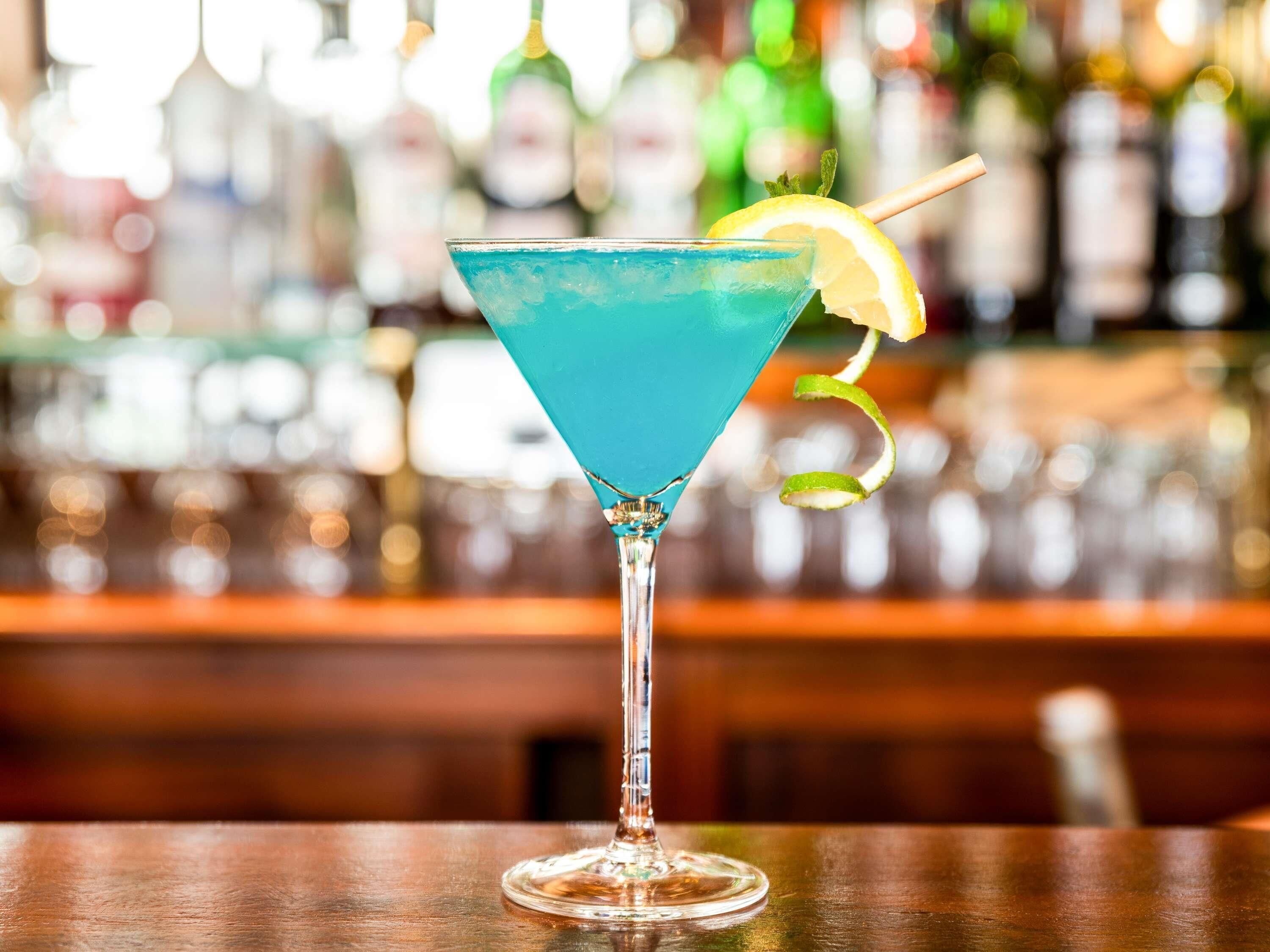Um cocktail azul num copo de martini com um toque de limão em cima de um balcão de bar.
