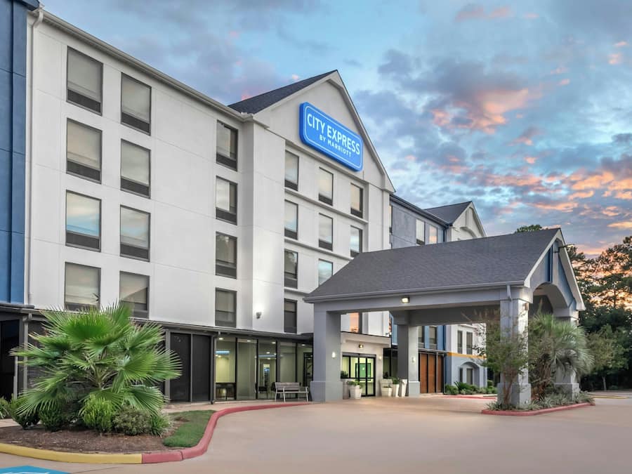 Um hotel moderno com fachada azul, entrada coberta e área ajardinada com plantas.