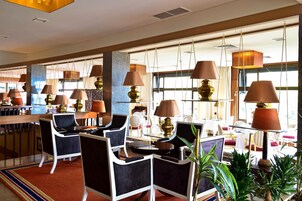 Um saguão de hotel com várias áreas de estar, incluindo mesas redondas e cadeiras, e um bar.