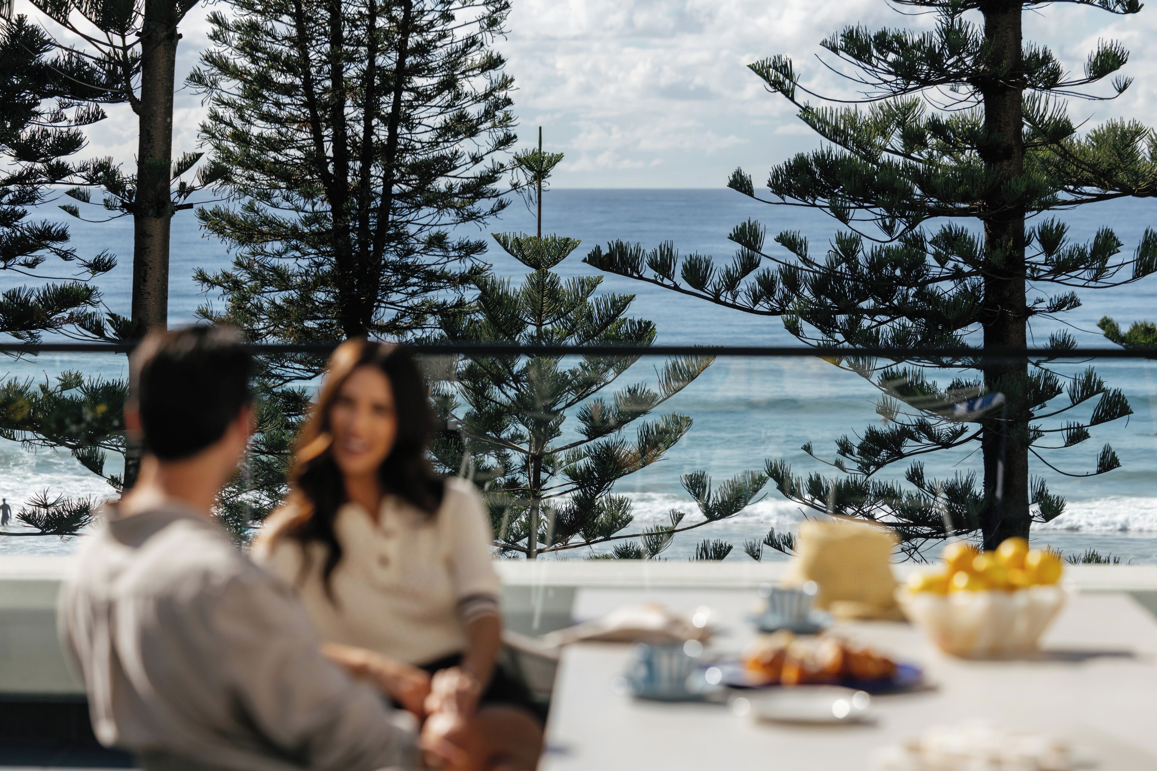 Uma área de refeições com vista para o oceano, com uma mesa posta e guarda-corrimão de vidro.