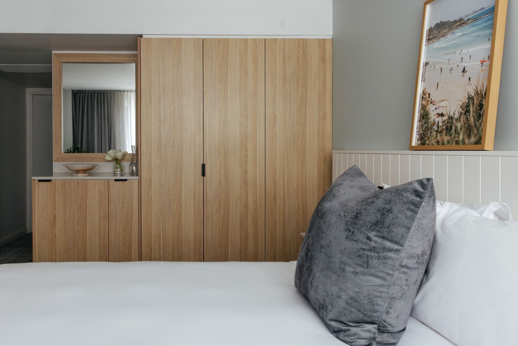 Quarto com cama, guarda-roupa espaçoso, espelho e quadro pendurado na parede.